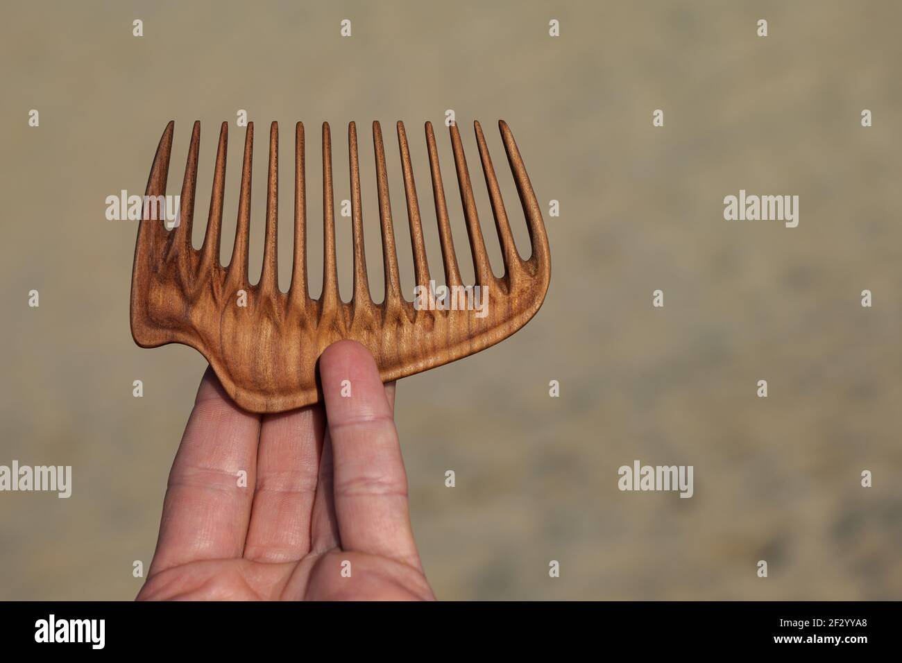 A hand holding natural wooden comb made of pear tree for scalp massage ...