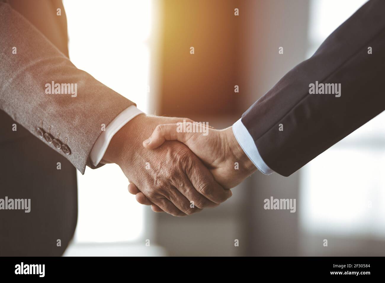 Business people standing and shaking hands in sunny office, close-up ...