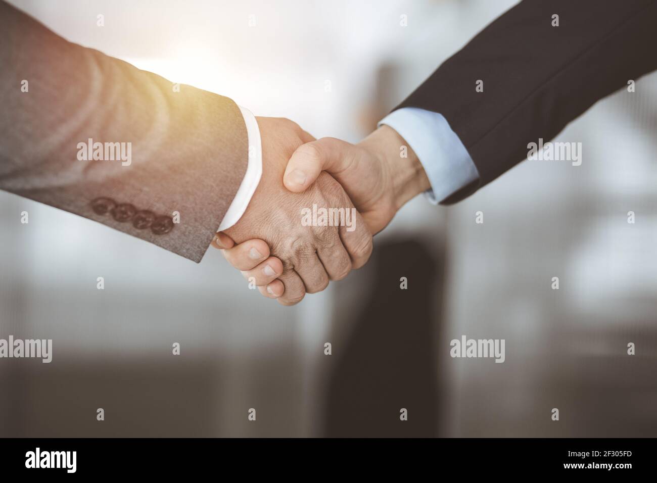 Business people standing and shaking hands in sunny office, close-up ...