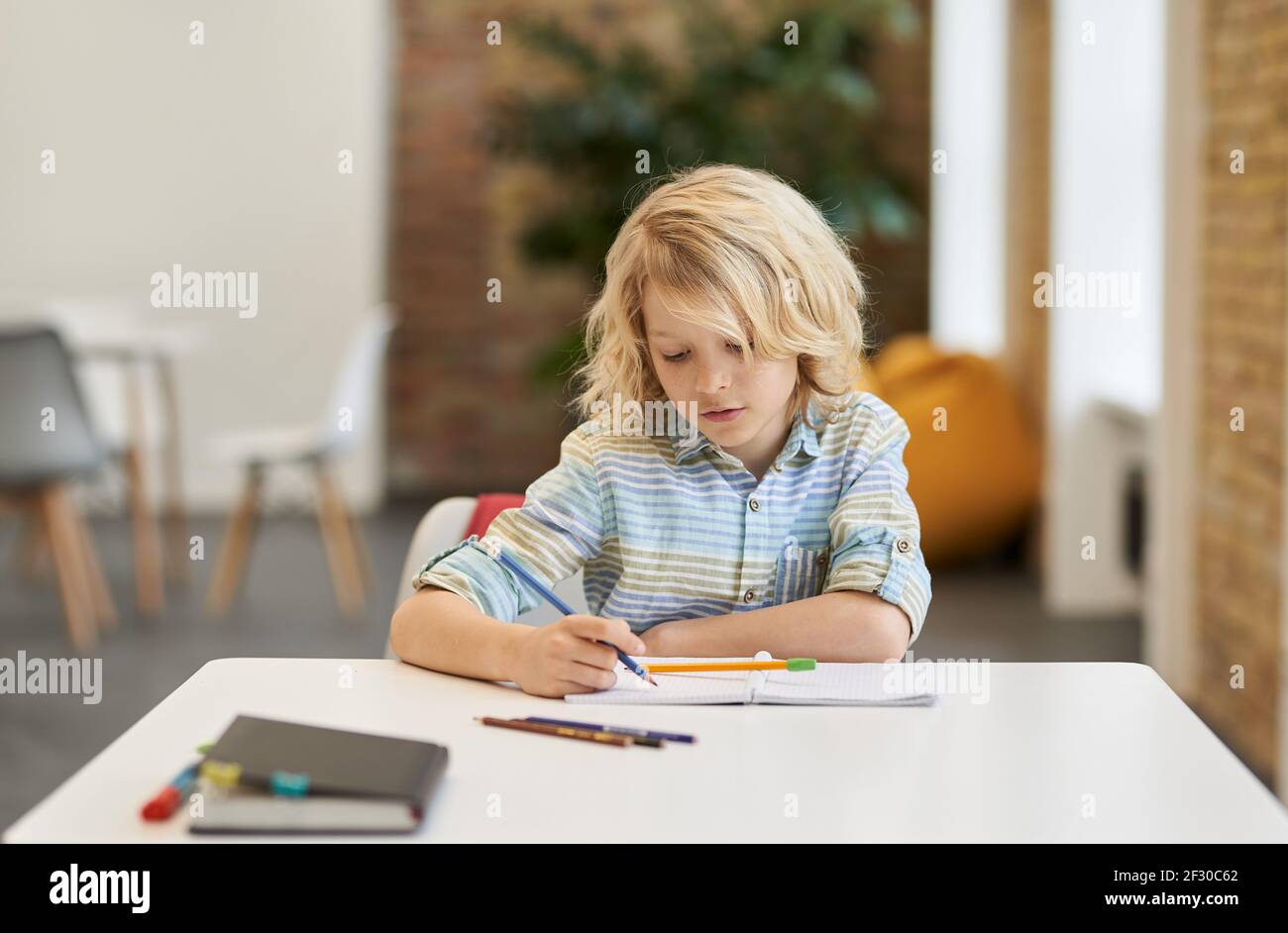 Doing assignment. Smart little school boy writing in his notebook while ...
