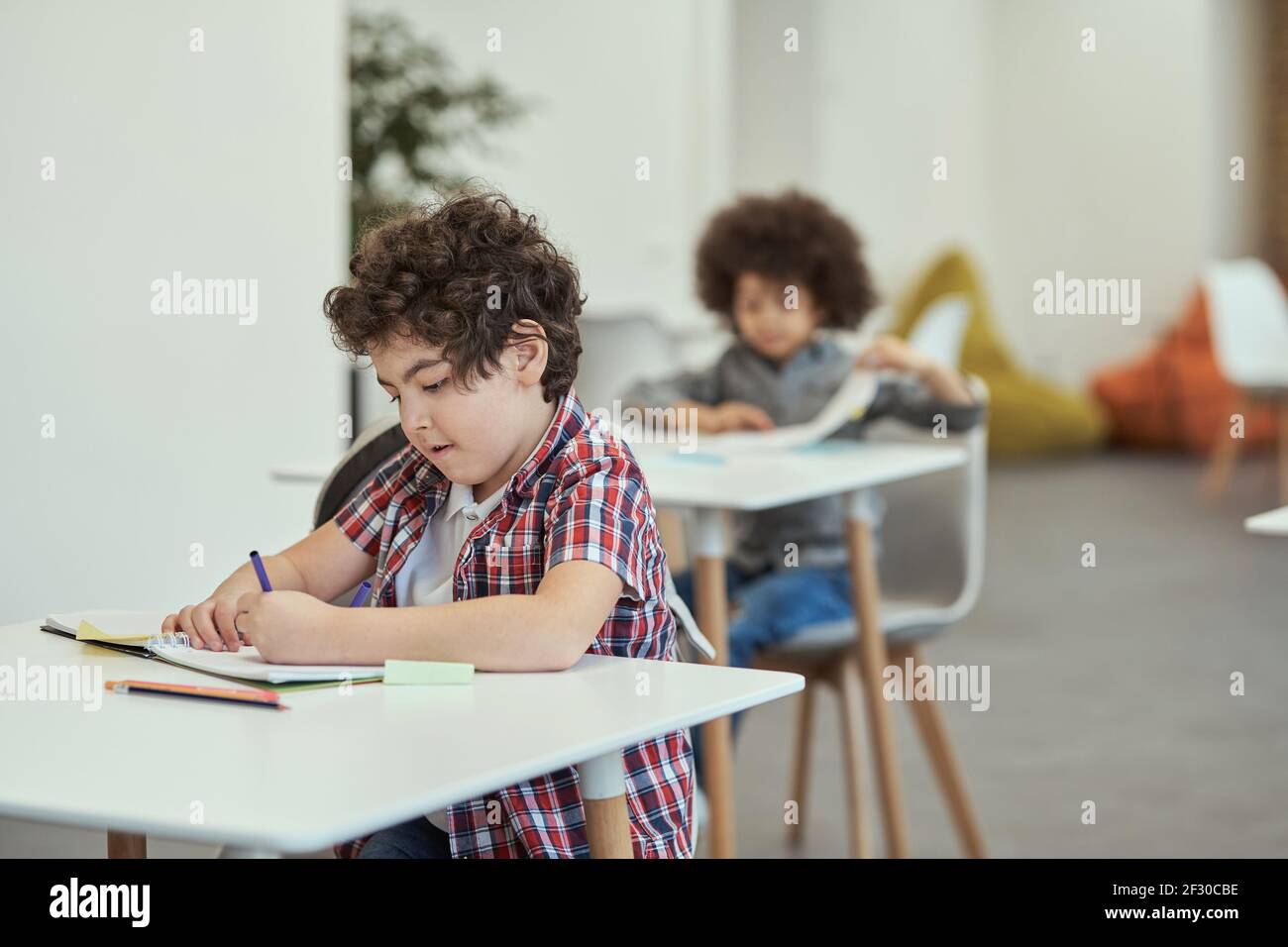 Learning process. Busy little school boy using pen for writing in ...