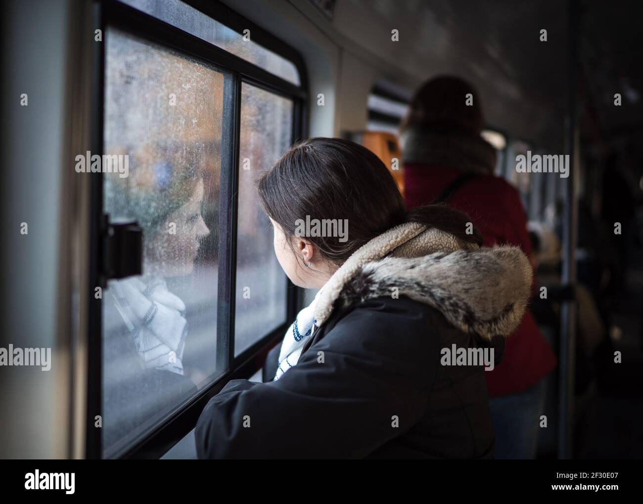 Woman standing on train looking out of window with face reflection ...