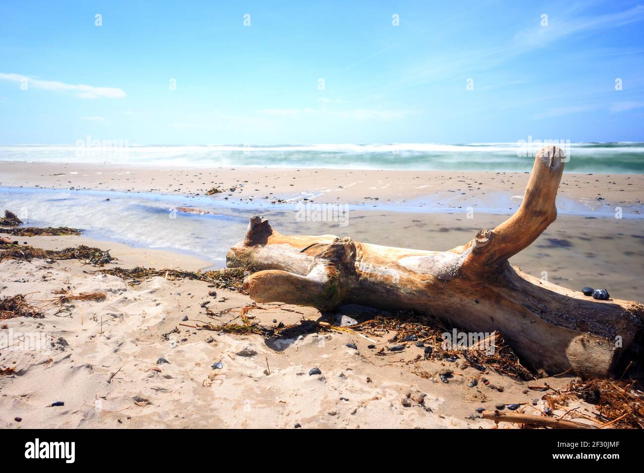 A log on the beach surrounded by the sea with long exposure under a ...
