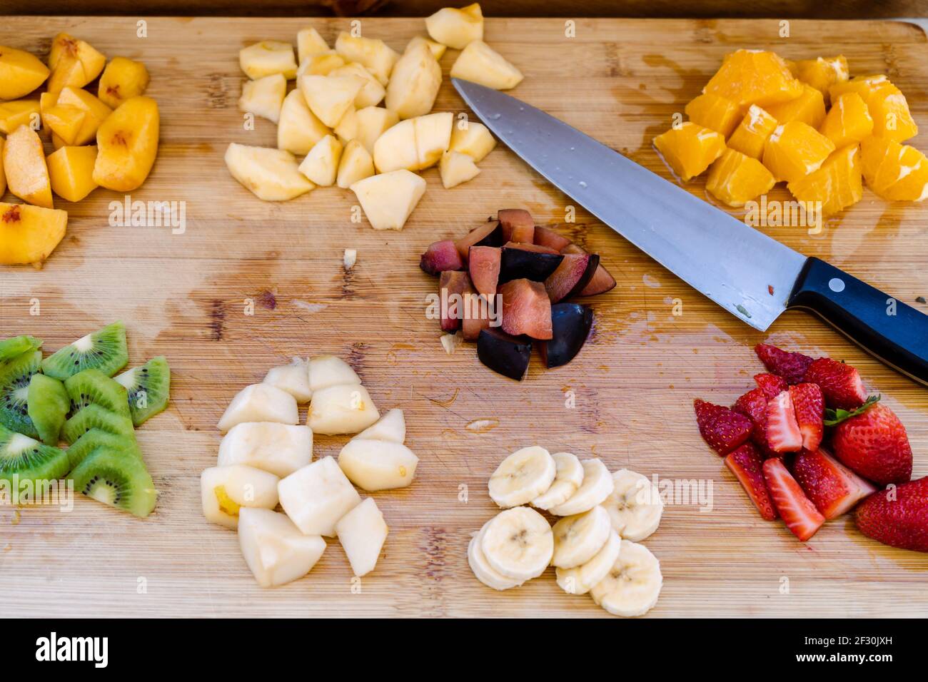 Chopped fruits arranged on cutting board on white wooden background ...