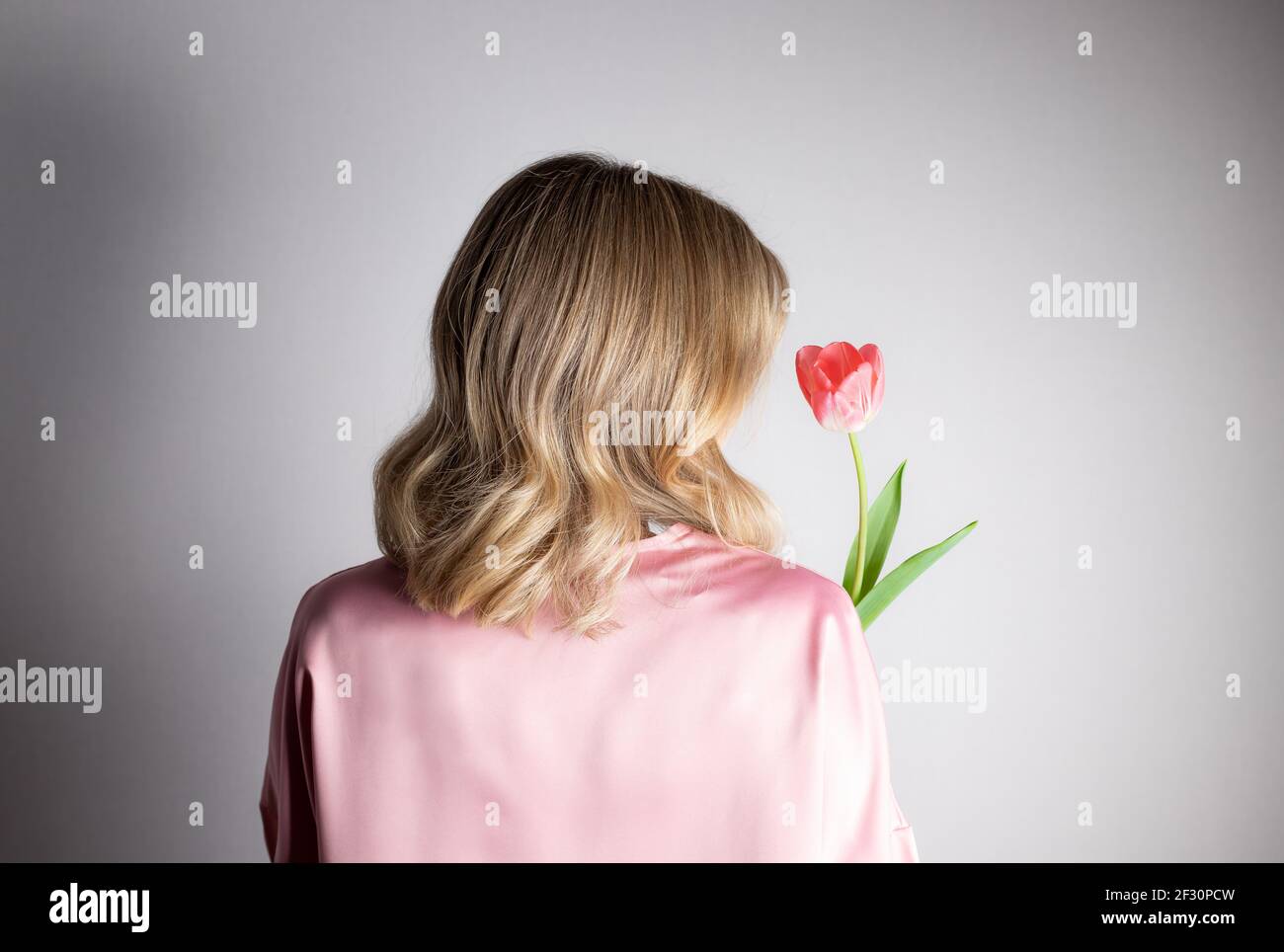 Back view of beautiful woman with tulip flower at gray wall Stock Photo ...