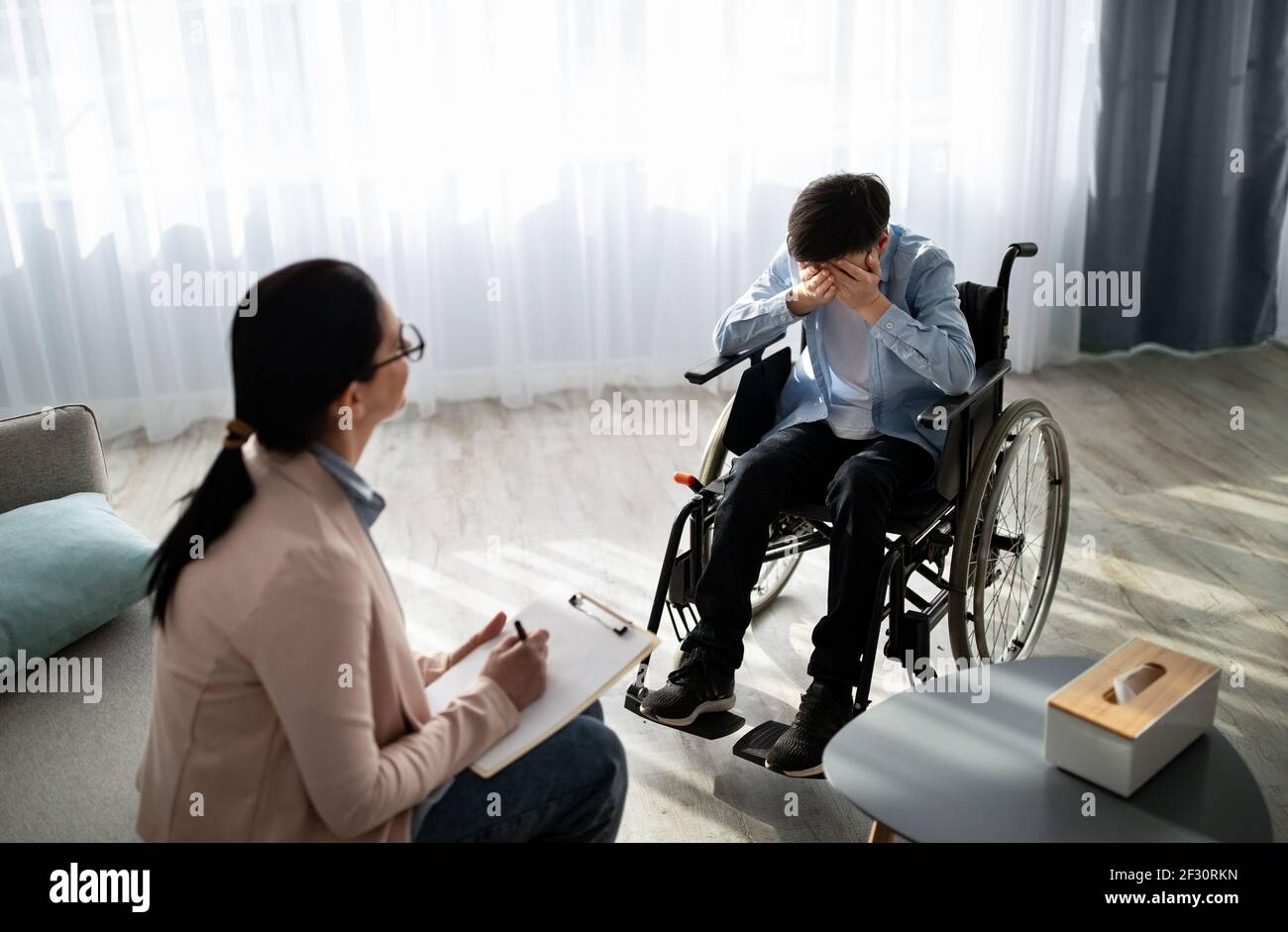 Above view of handicapped teen boy in wheelchair crying on consultation ...