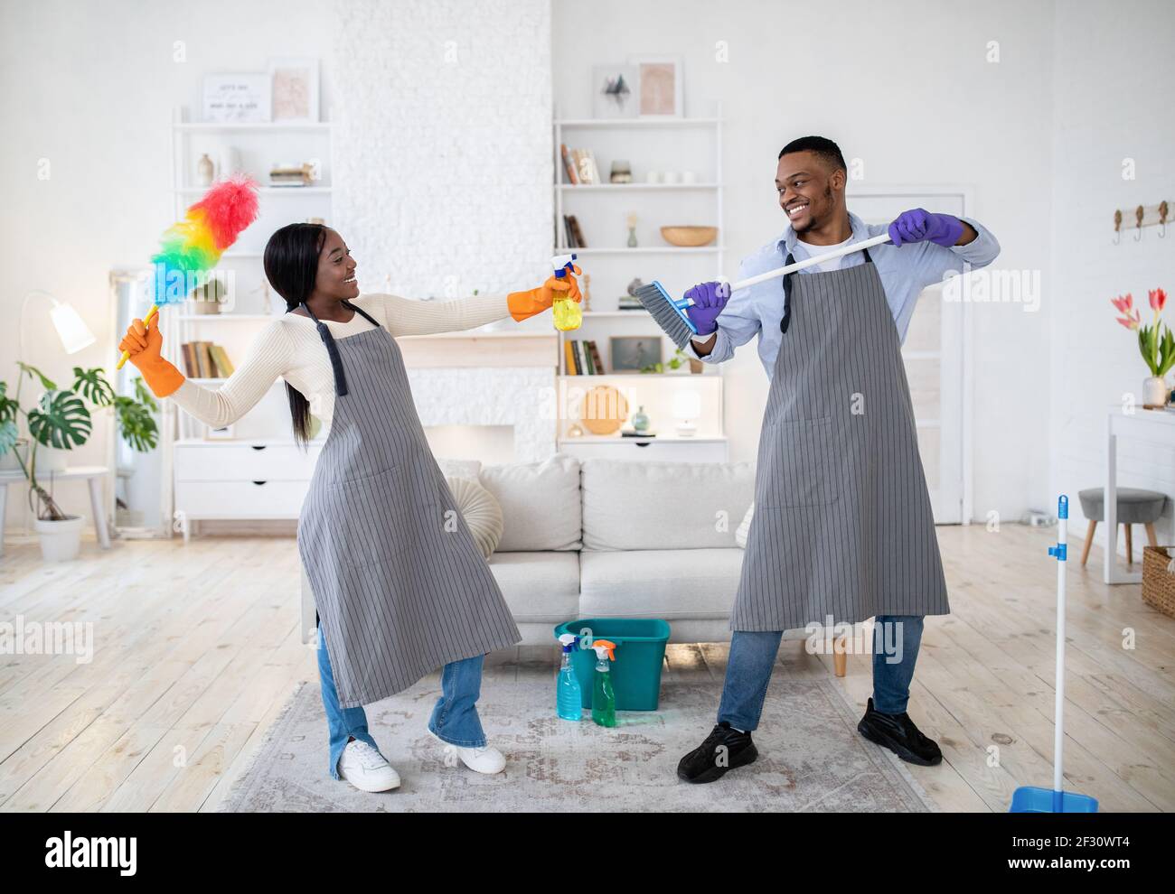 Playful black couple having mock fight with mop and detergent, being ...