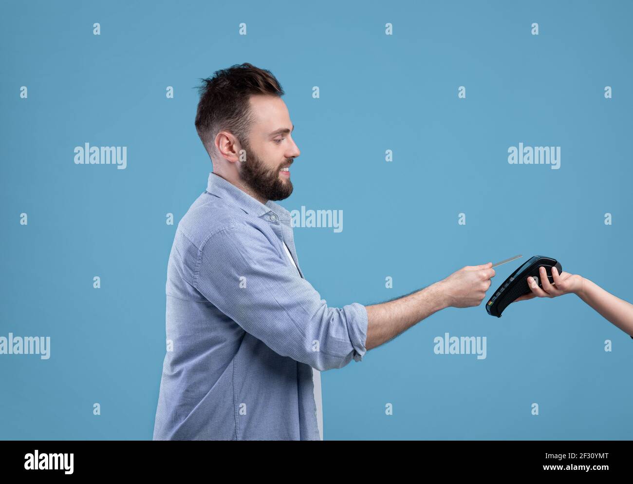 Side view of smiling young man paying with credit card on payment ...