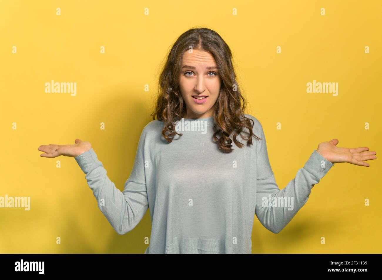 Uncertainty concept. A young curly brunette woman spreads her arms and ...