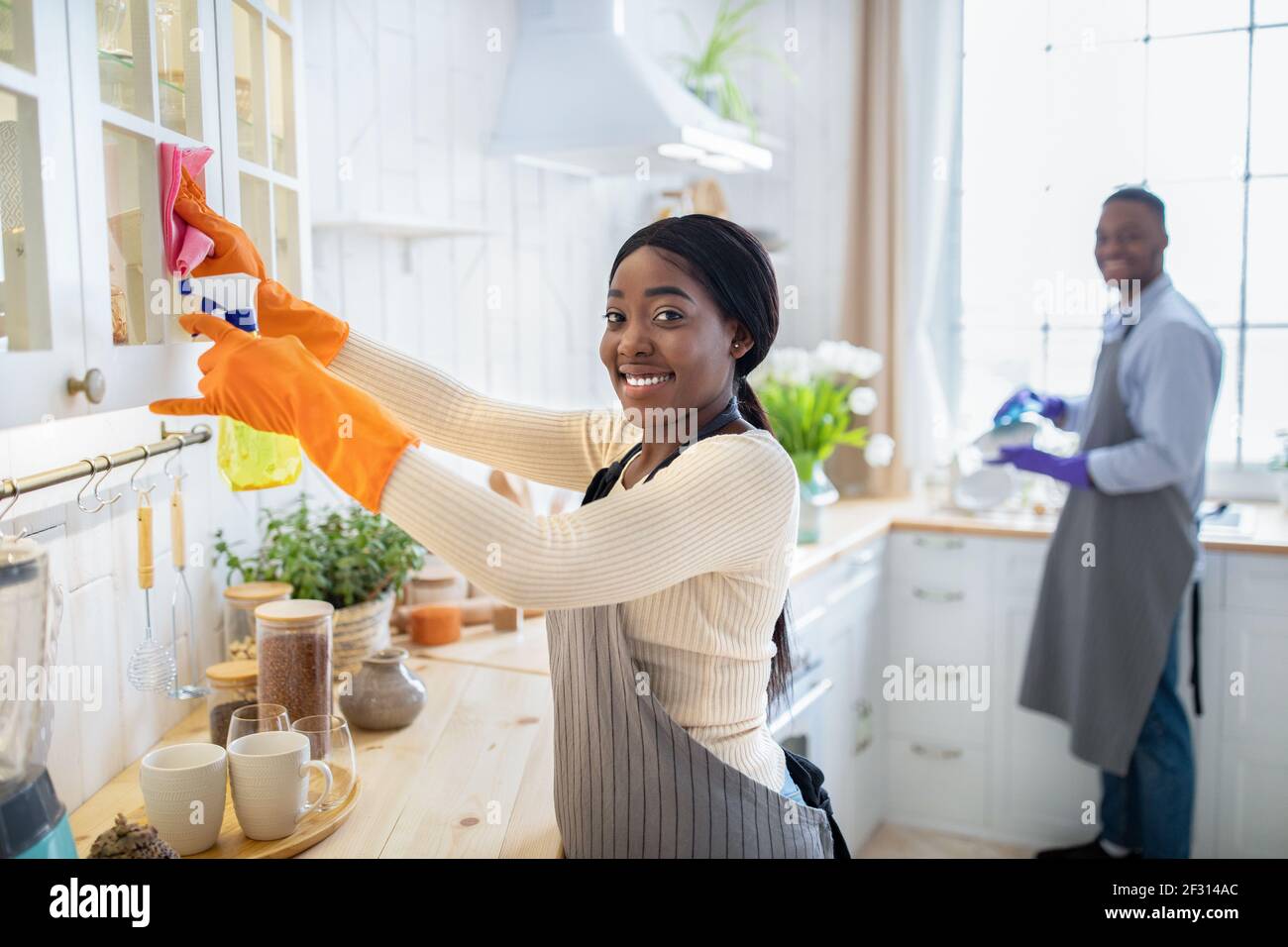 Happy black lady cleaning kitchen cabinet, her husband washing dishes ...