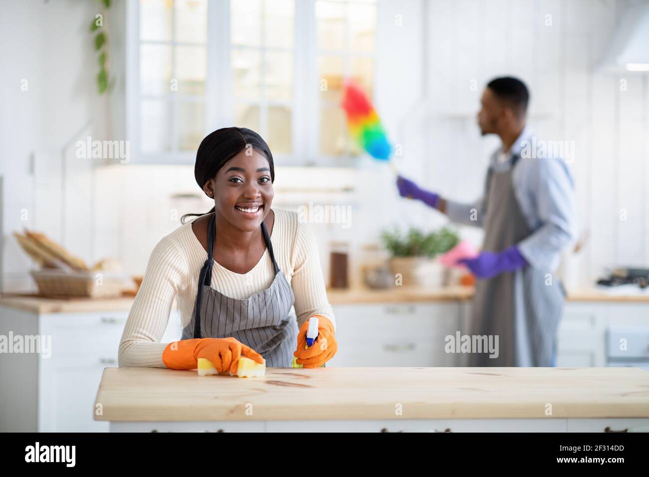 Happy African American woman wiping kitchen table while her husband ...