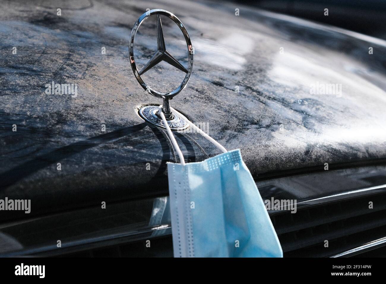 A face mask hangs from the star of a mercedes car Stock Photo - Alamy