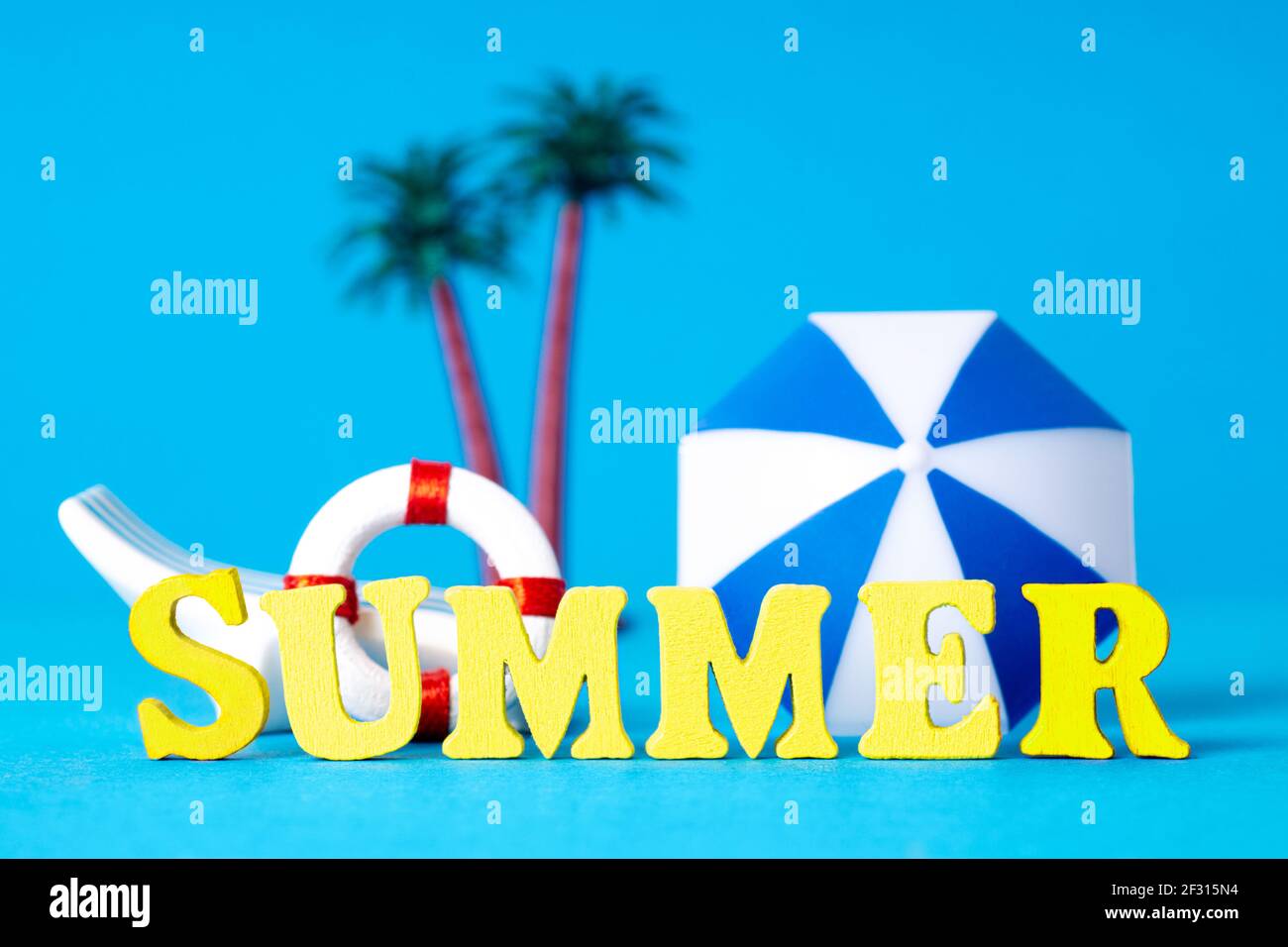 Word SUMMER made of yellow wooden letters with blurred toy palm trees ...