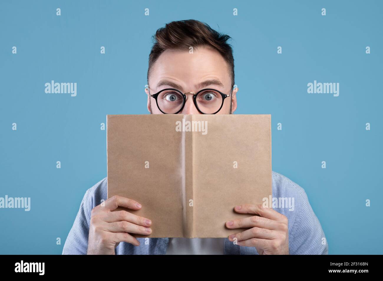 Shocked young guy in glasses reading book, opening his eyes wide in ...