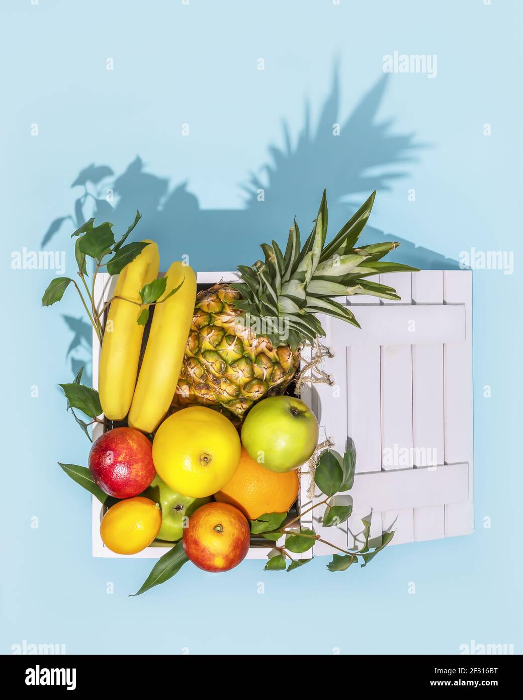 Fresh tropical fruits in a wooden box with dark shadows on a blue ...