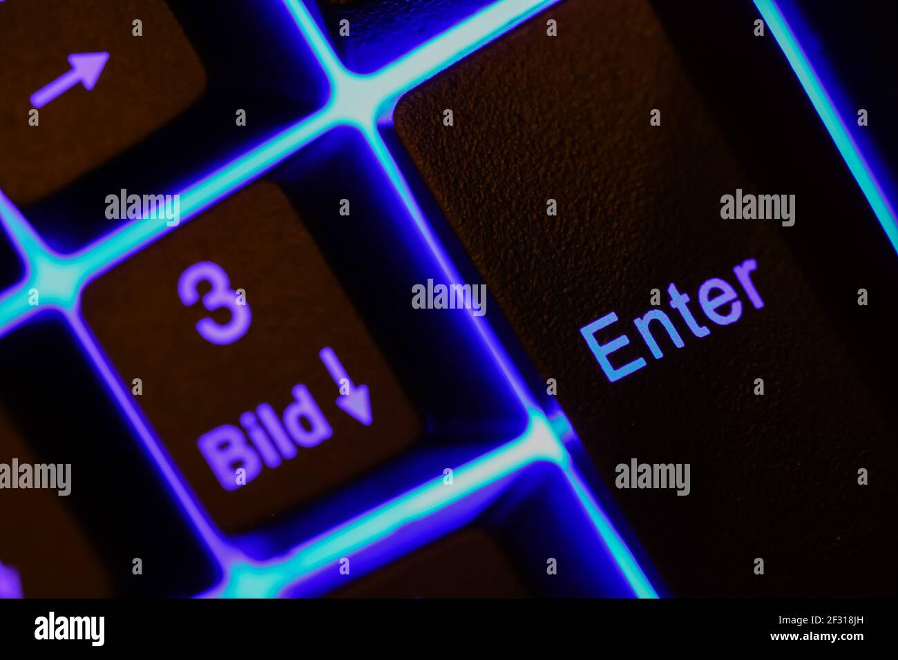 Macro closeup of blue illuminated enter key on computer keyboard ...