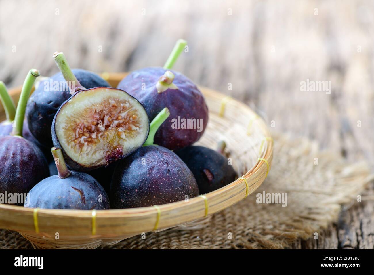 Fresh purple fig fruit and slices isolated in bamboo basket on old wood ...
