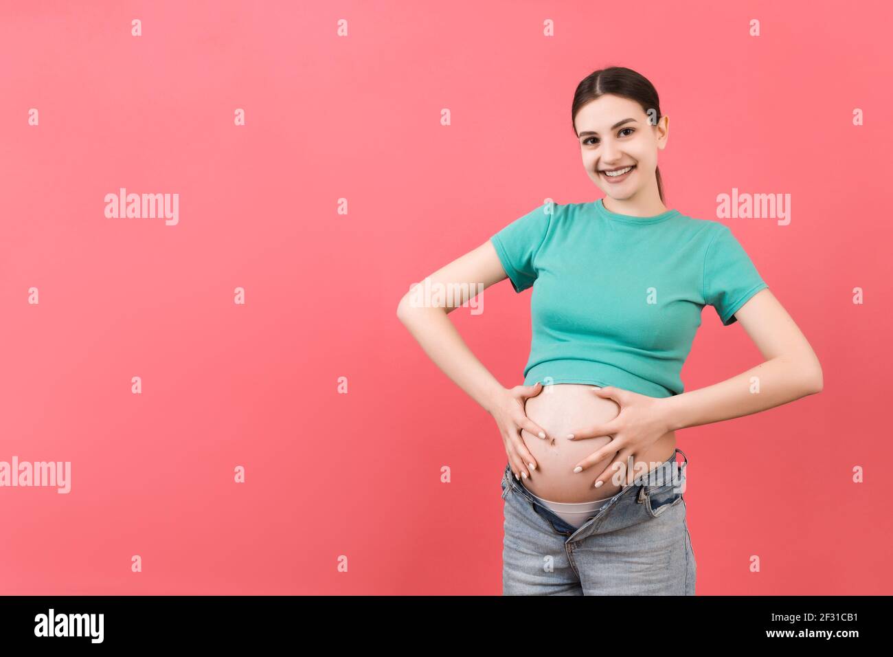 pregnant woman dressed in opened jeans scratching her belly at colorful ...