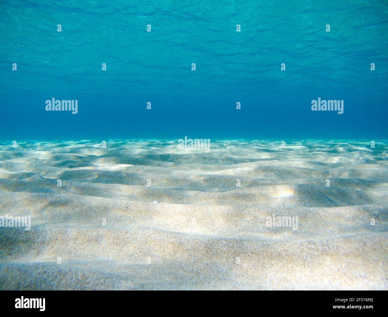 Underwater view on sand sea bottom close-up in sun beam reflections in ...