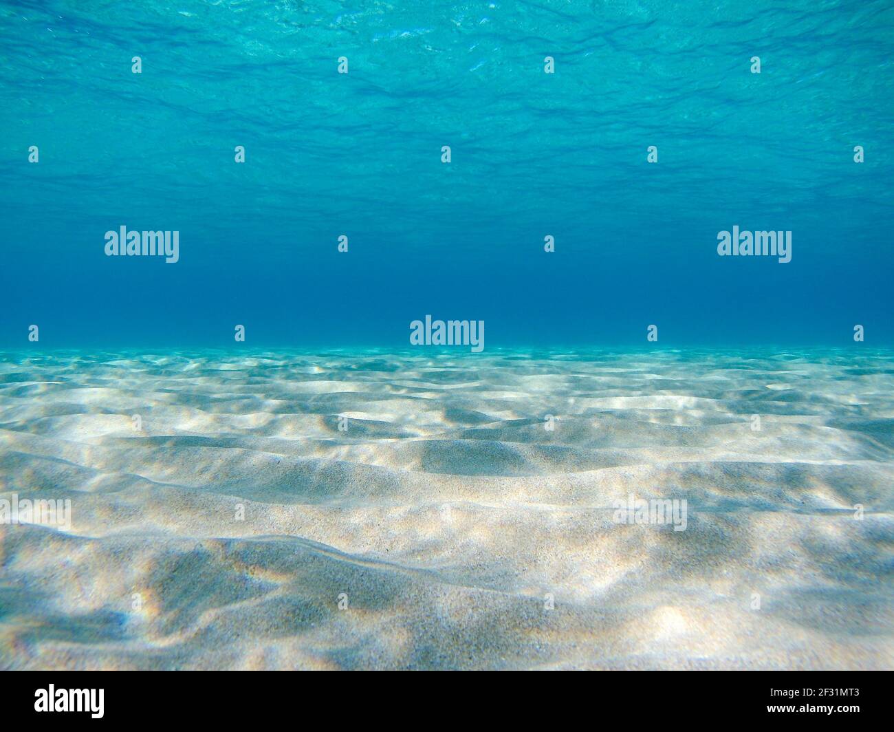 Underwater view on sand sea bottom close-up in sun beam reflections in ...