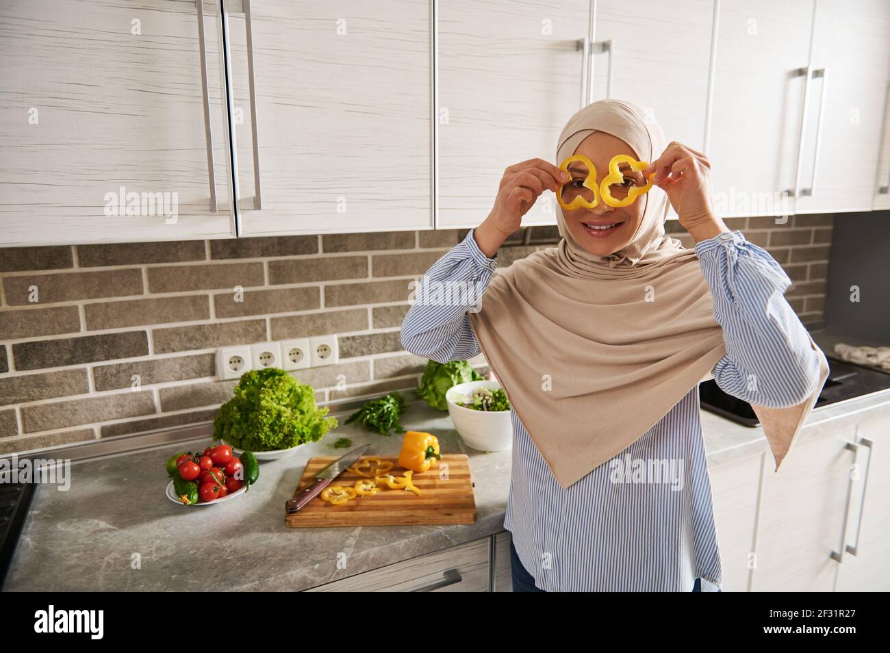 Muslim Arab woman in hijab looks through slices of yellow pepper ...
