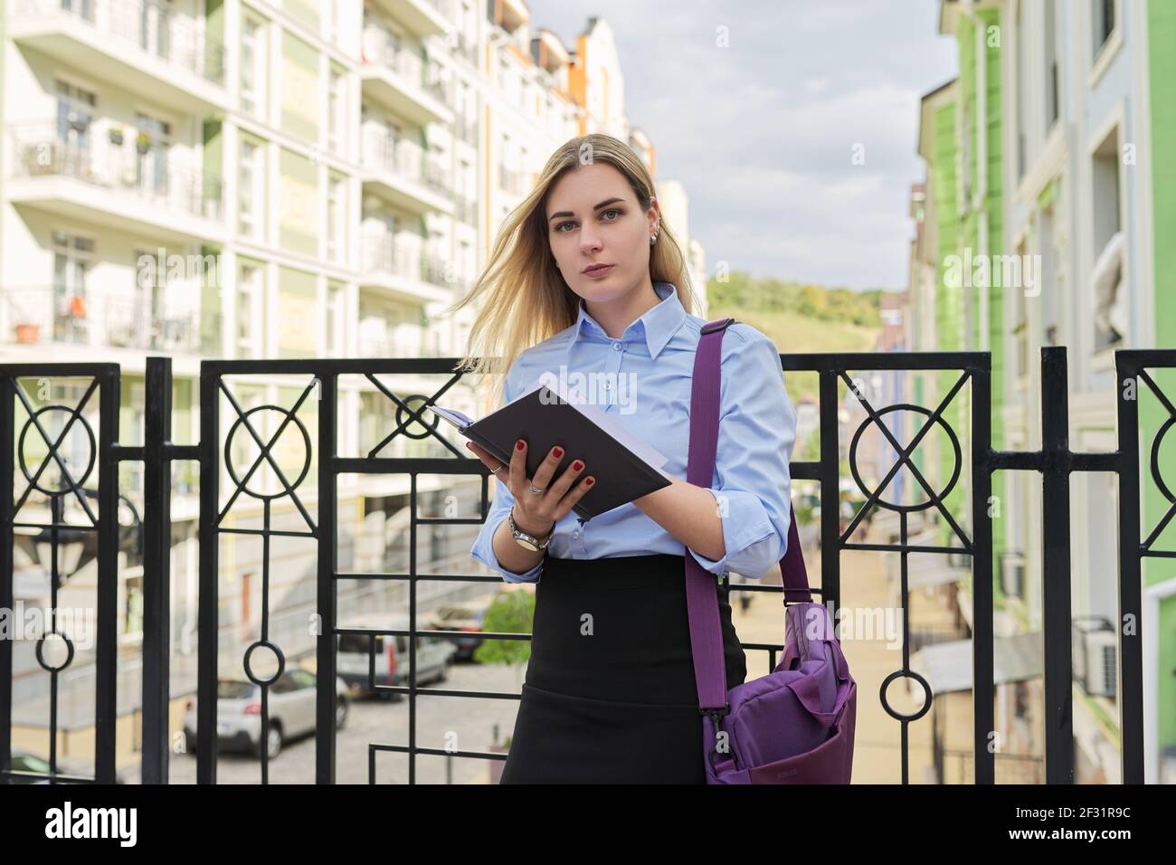 Young businesswoman in blue shirt with laptop bag writing in business ...