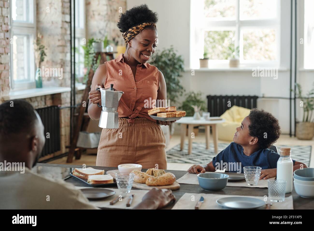 Young smiling mother in casualwear passing homemade waffles to her cute ...