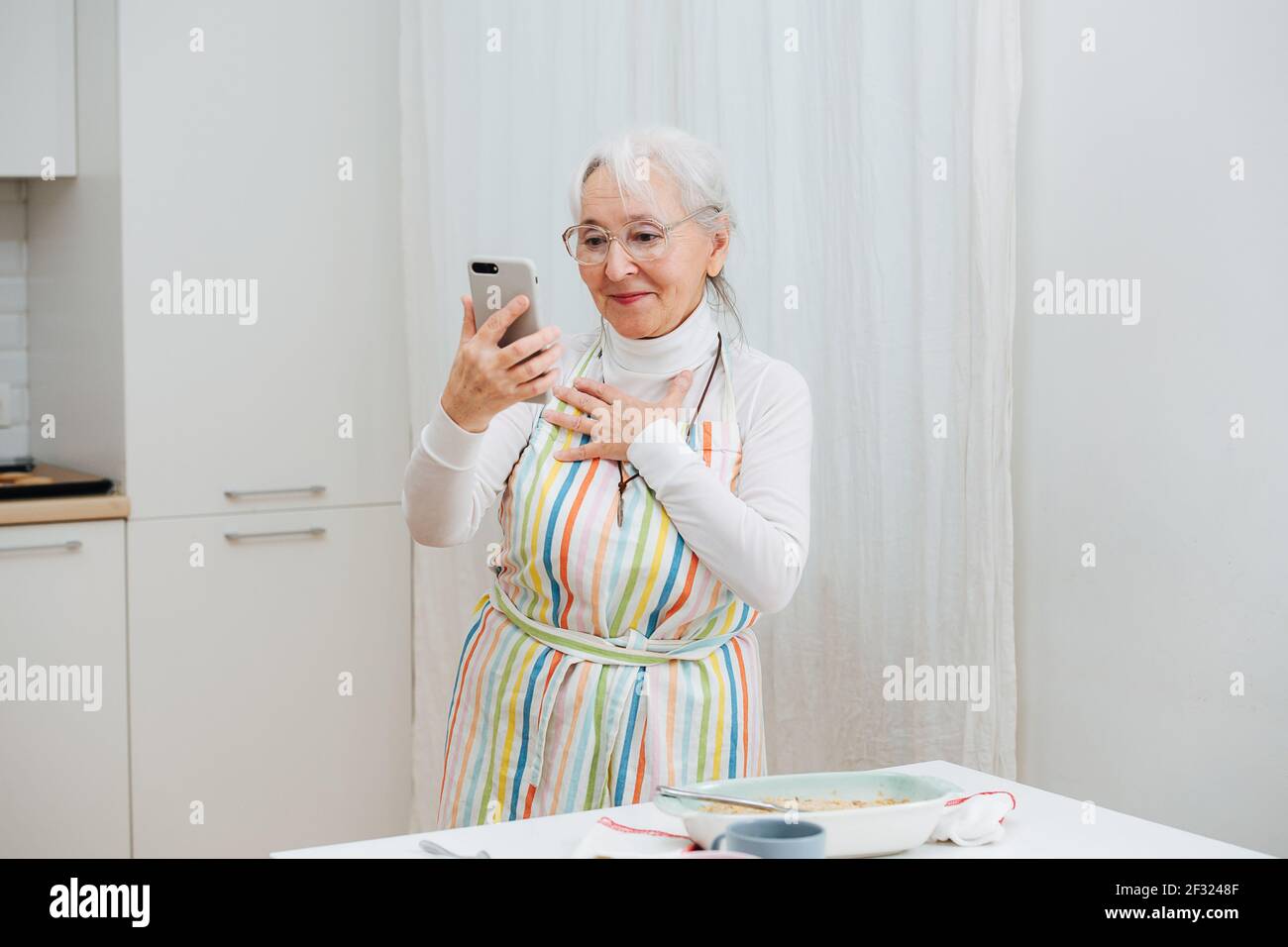 Friendly granny talking via video call on the phone in the kitchen ...