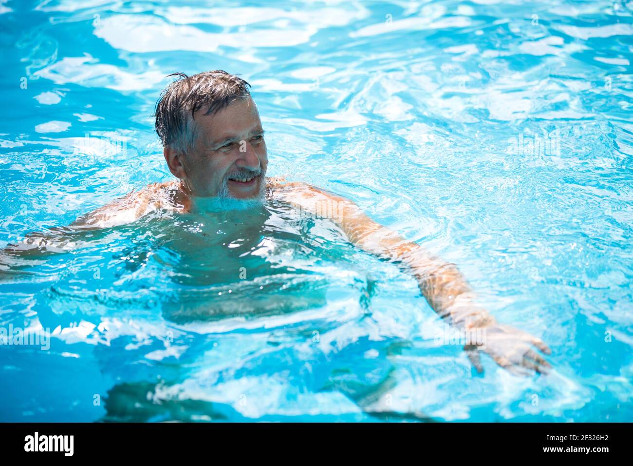 Senior man in his home swimming pool, enjoying the deserved retirement ...