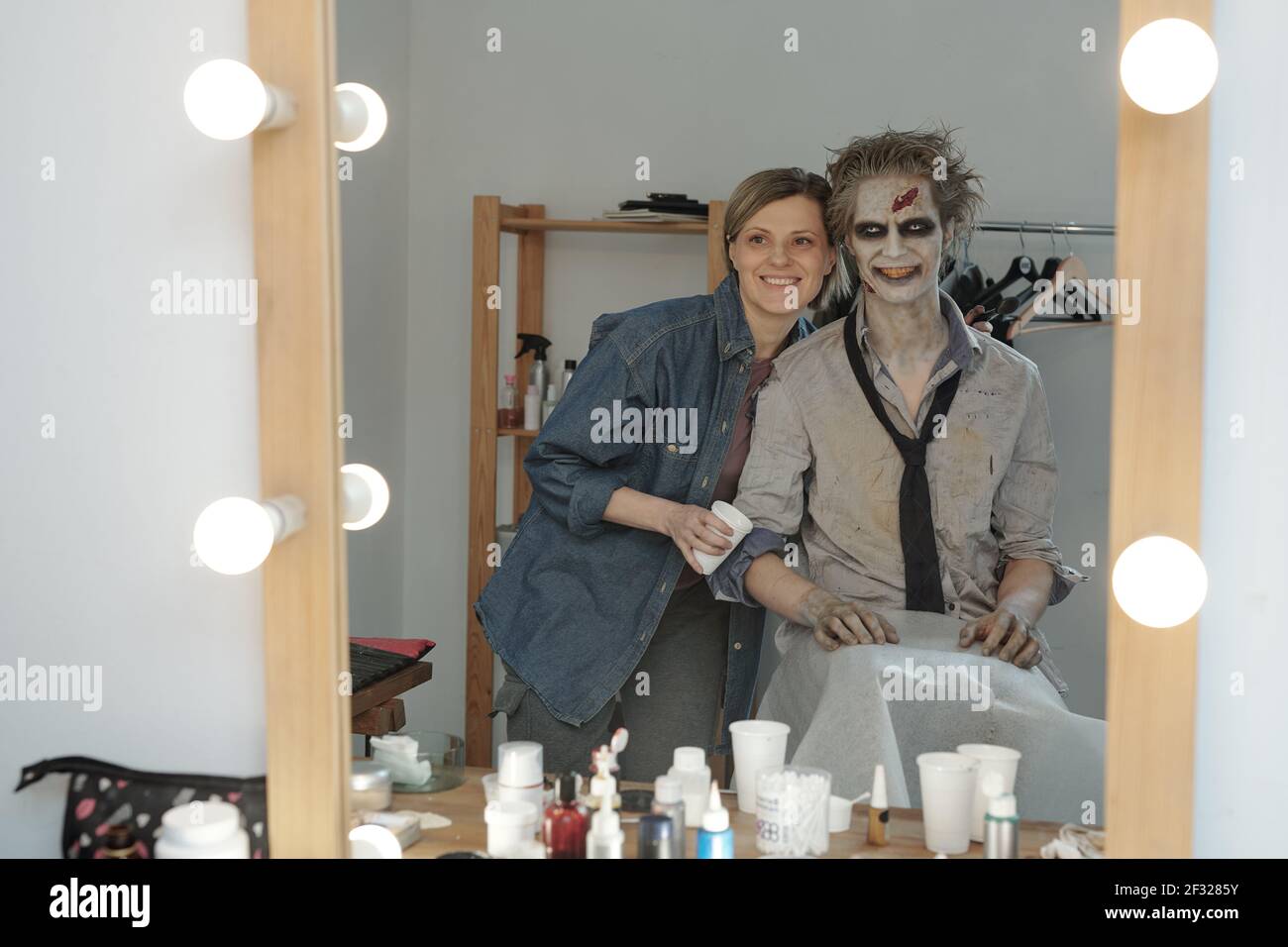 Reflection in mirror of female makeup artist and young grinning spooky ...