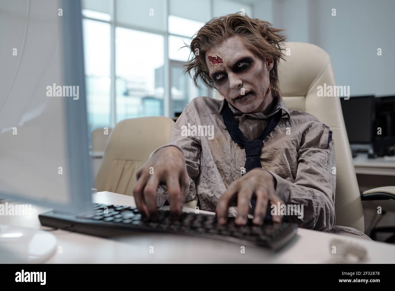 Spooky businessman with zombie body painting looking at computer screen ...