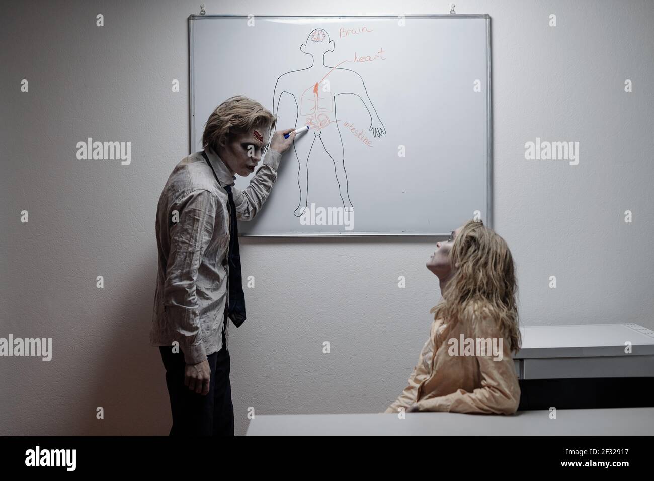 Young spooky zombie businessman looking at female colleague while ...