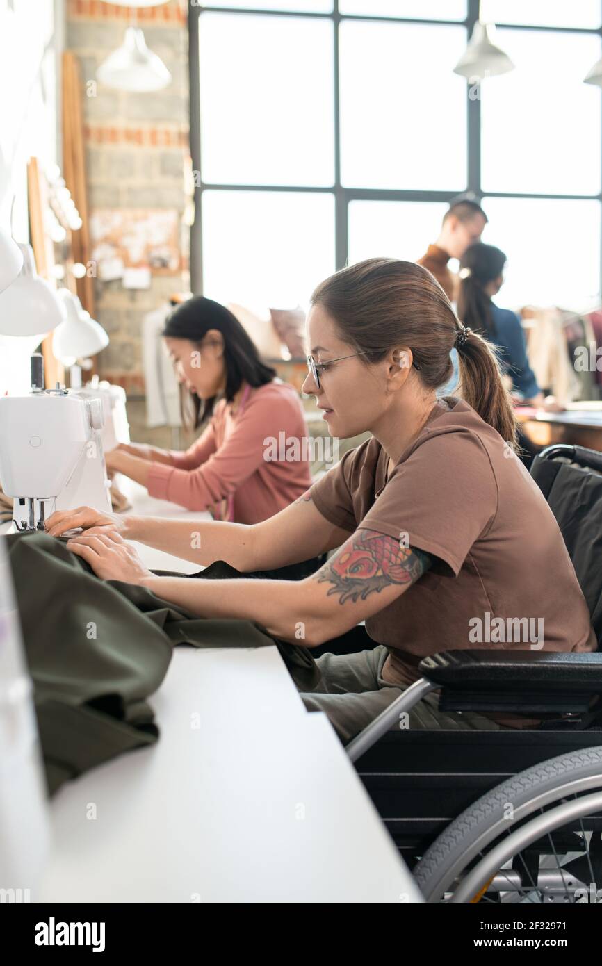 Young disable seamstress sitting in wheelchair by workplace in front of ...