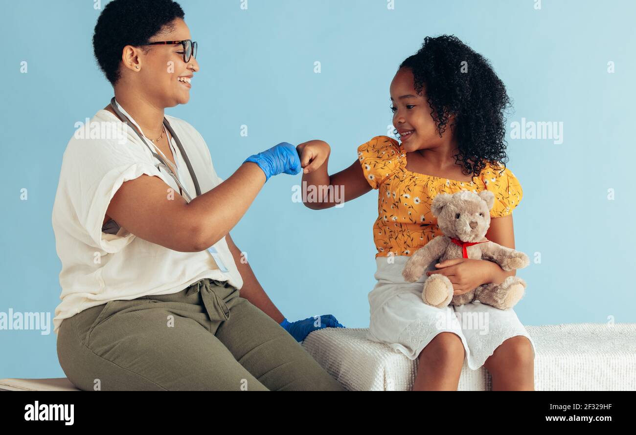 Doctor giving fist bump to girl sitting in clinic. Girl visiting doctor ...
