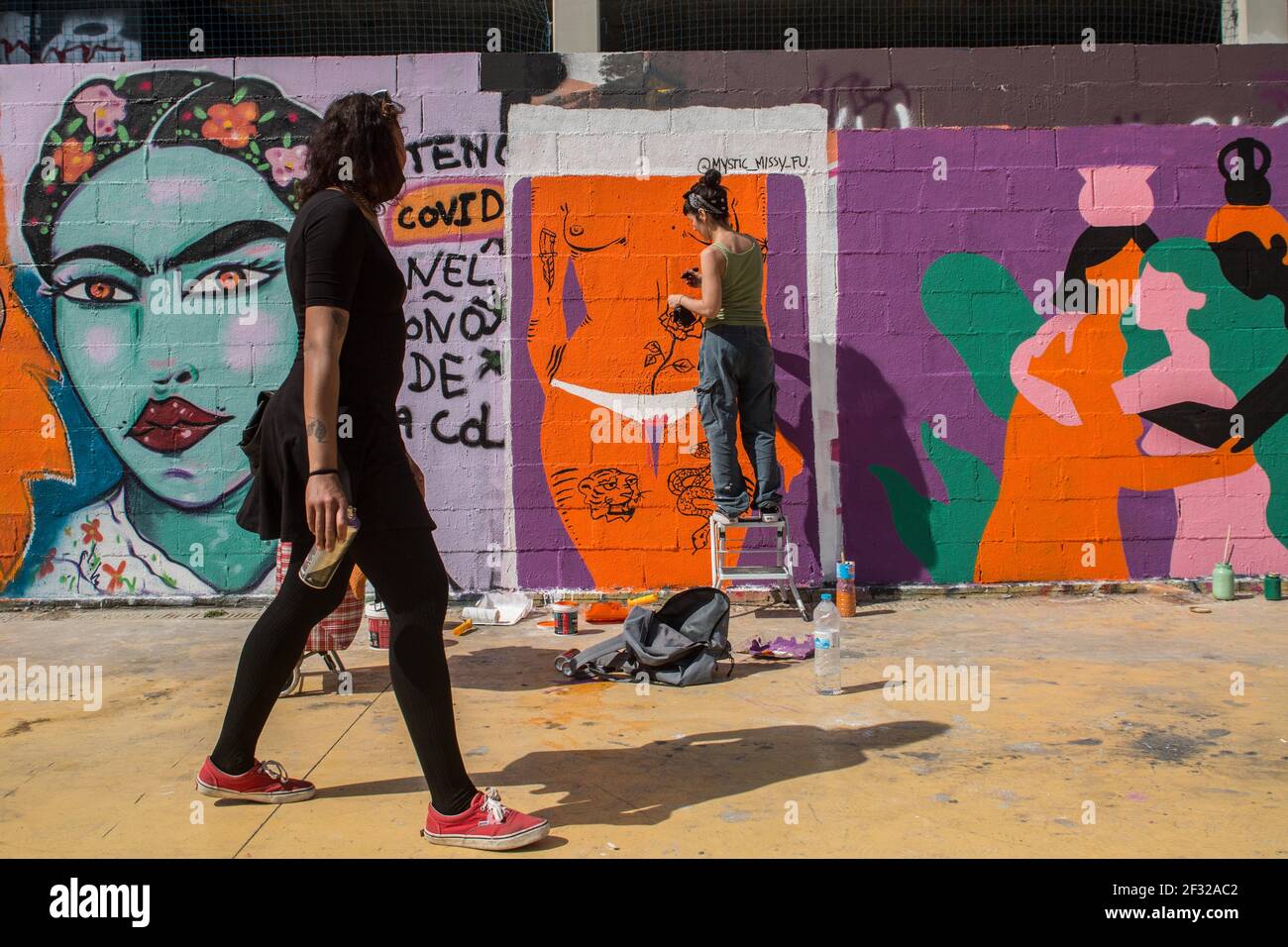 A woman walks by a demonstrator graffiti writing on the wall during ...