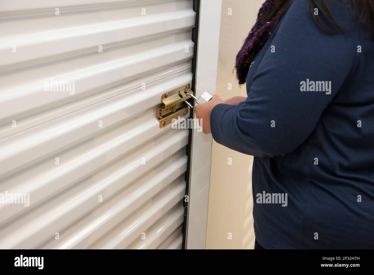 A hand turns a padlock with a key at a storage unit or locker for ...