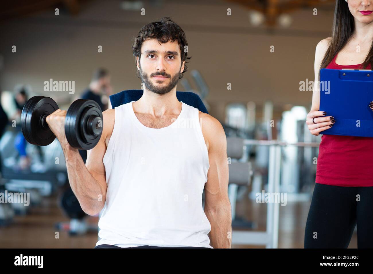 Man working out in a gym while his personal trainer looks at the ...