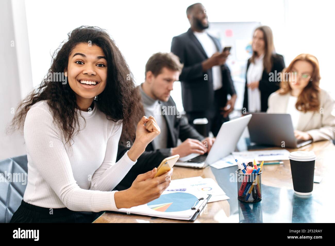 Excited young african american lady using smartphone, sitting in office ...