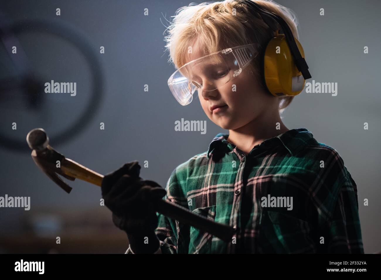 cute blond child boy with a hammer in hand in a carpenter's workshop ...