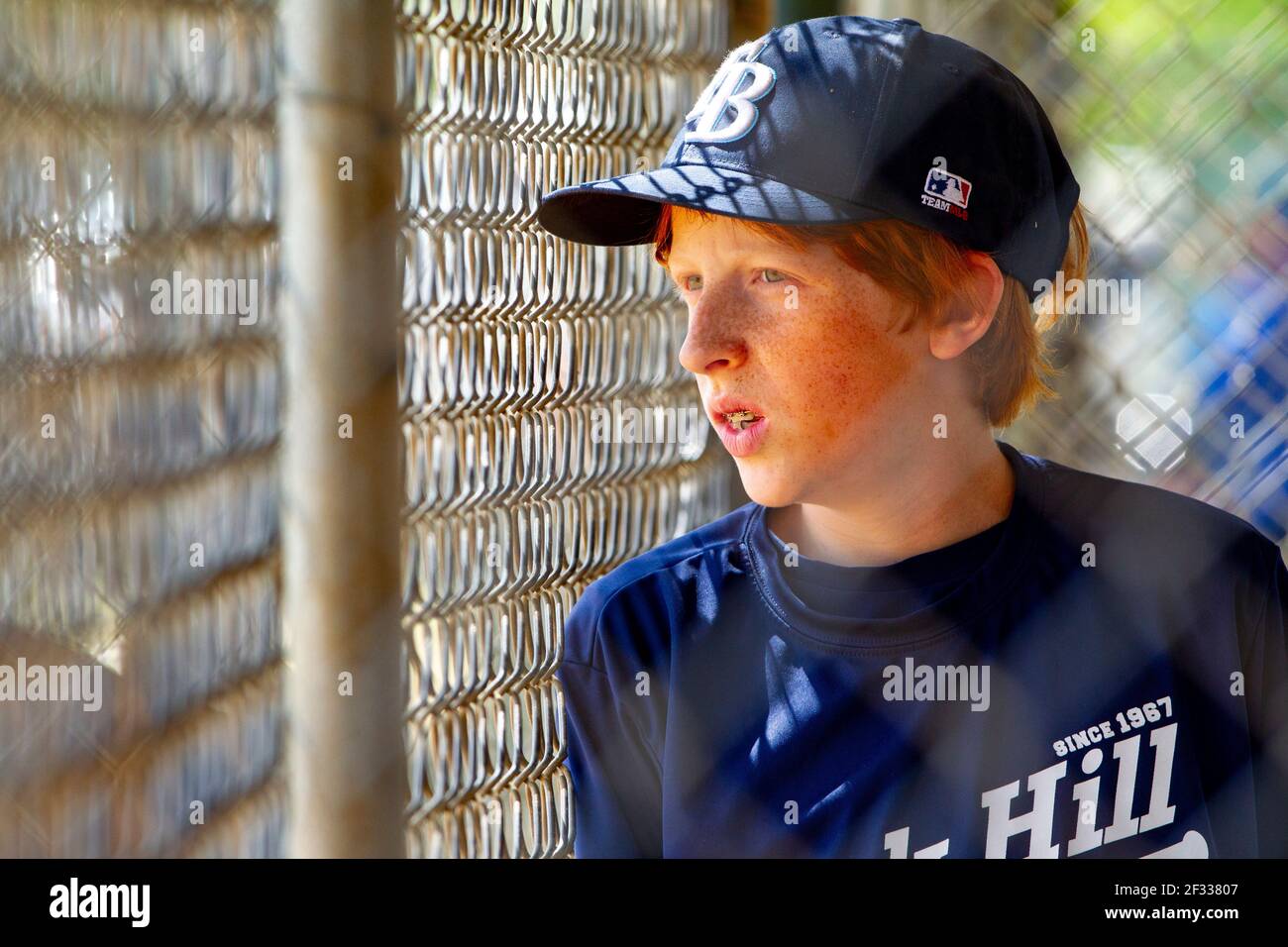 A young red-headed baseball player looks out onto the field during a ...