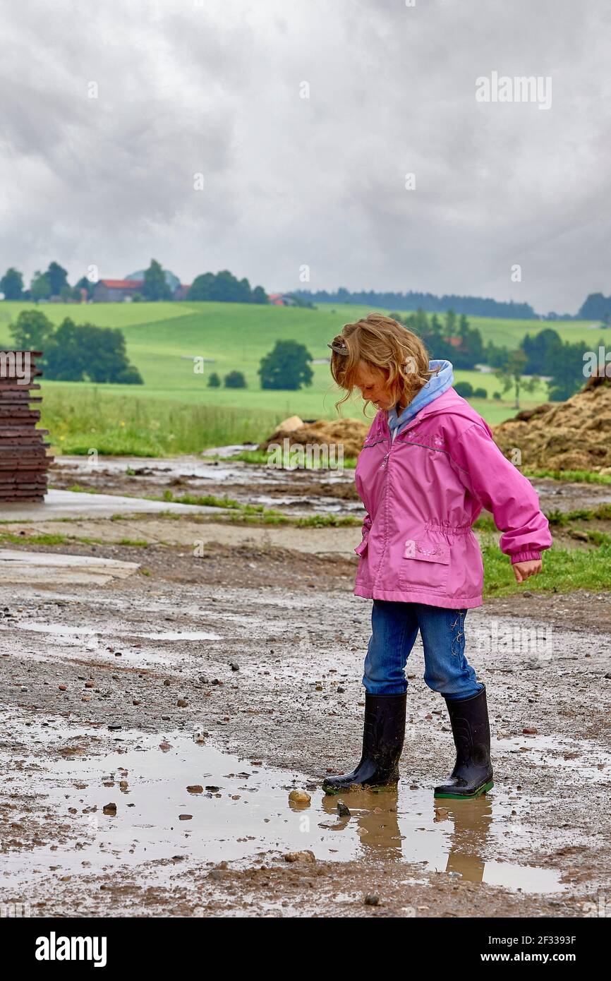 Full body girl in pink raincoat and rubber boots playing in puddle of ...
