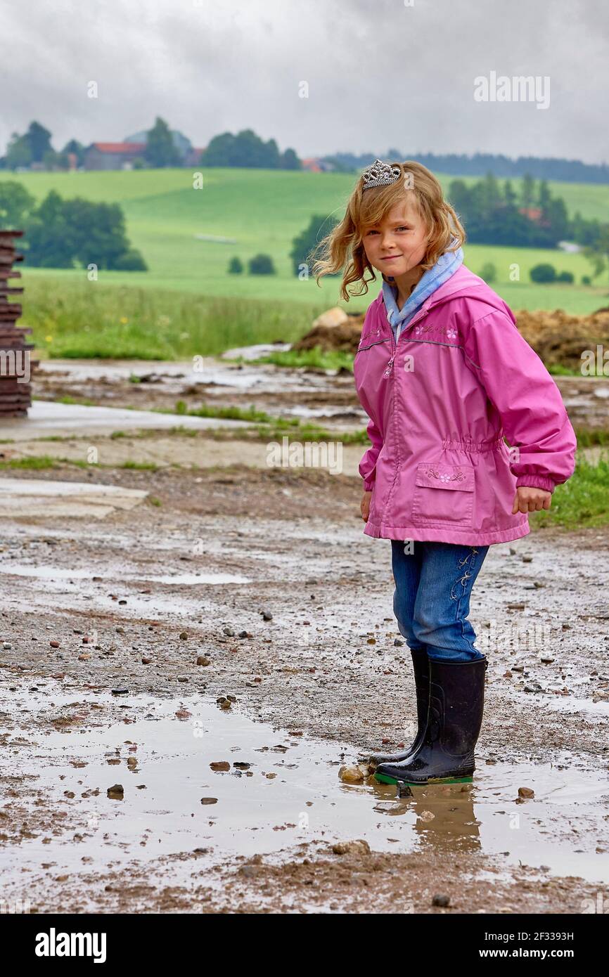 Full body girl in pink raincoat and rubber boots playing in puddle of ...