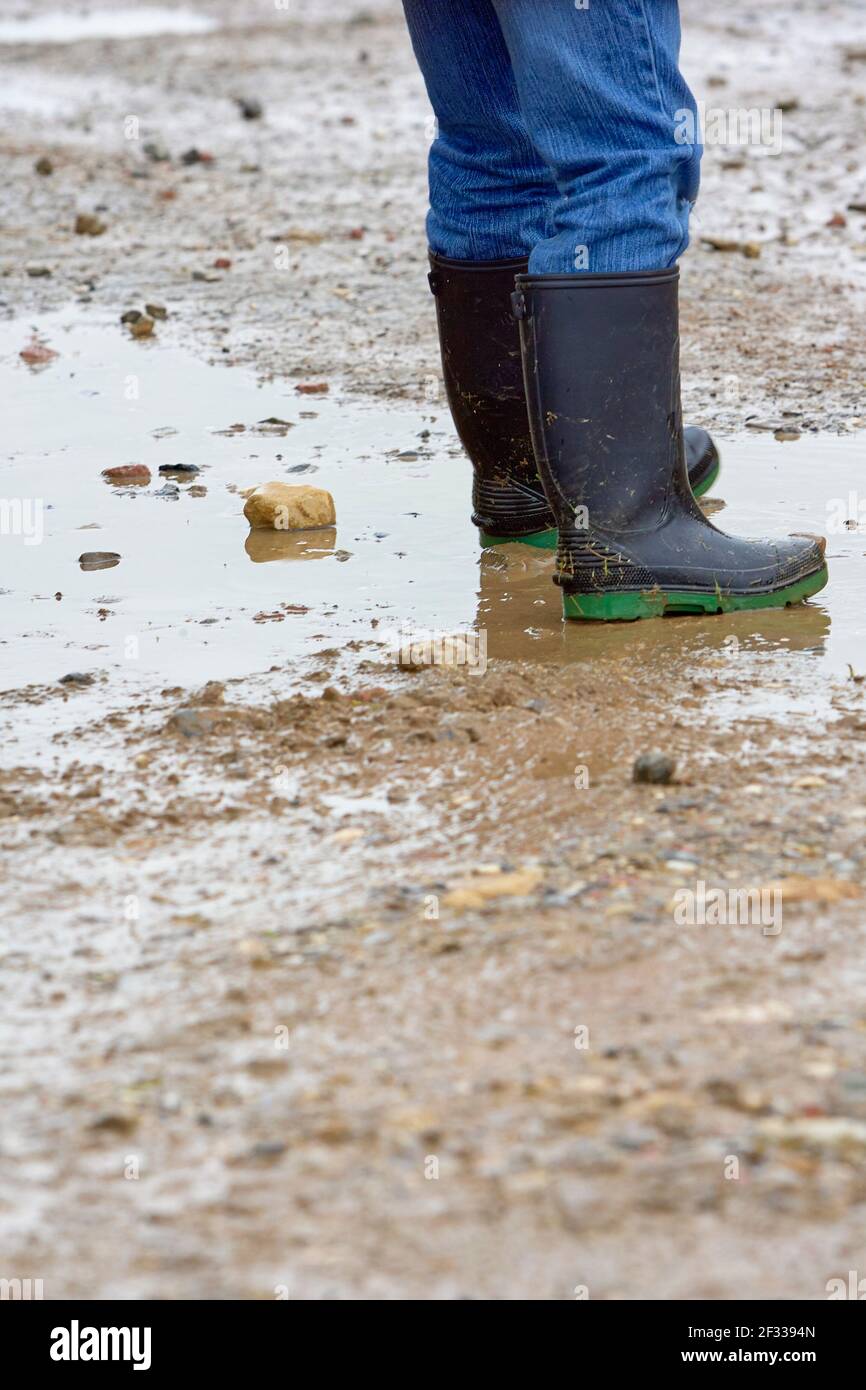 Young blond girl playing in a muddy puddle outside while it is raining ...