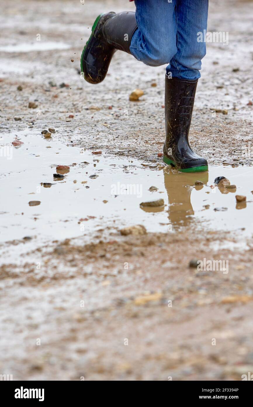 Young blond girl playing in a muddy puddle outside while it is raining ...