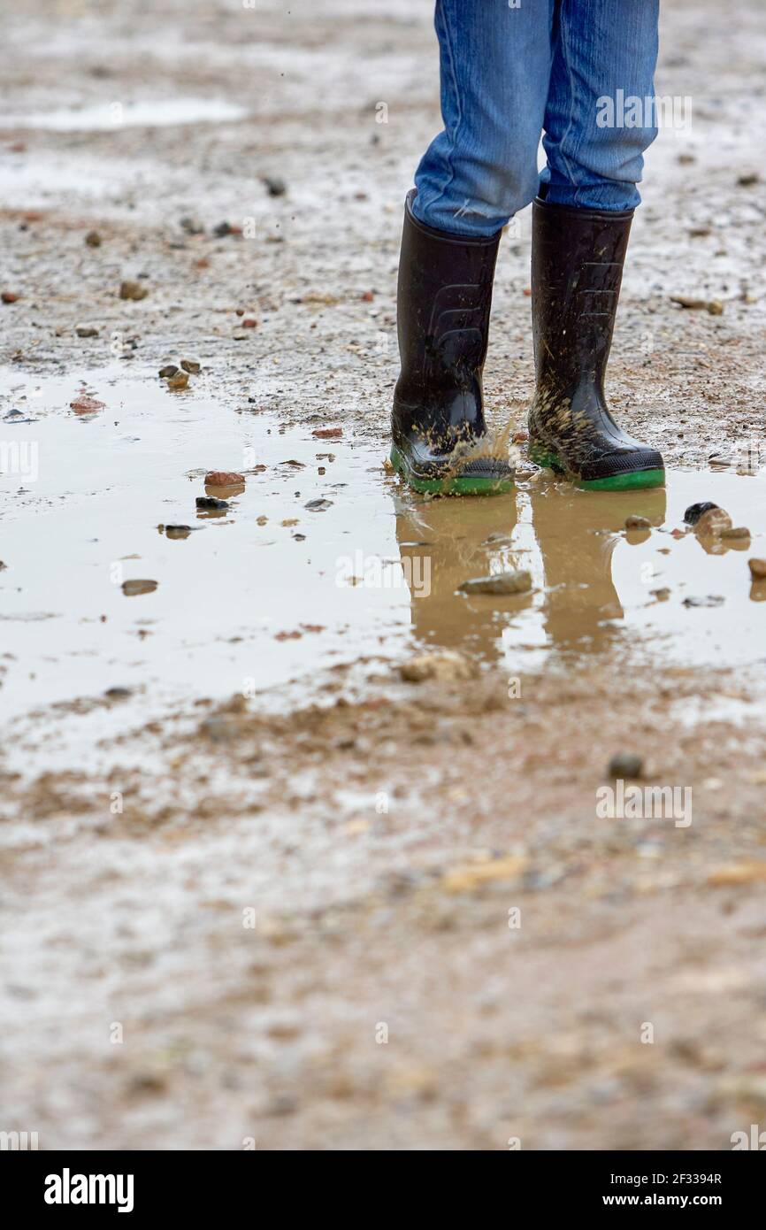Young blond girl playing in a muddy puddle outside while it is raining ...