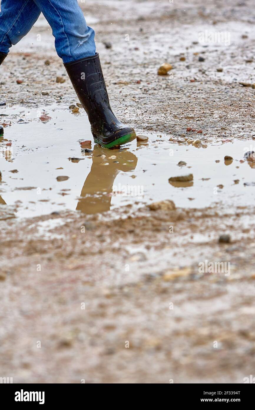 Young blond girl playing in a muddy puddle outside while it is raining ...