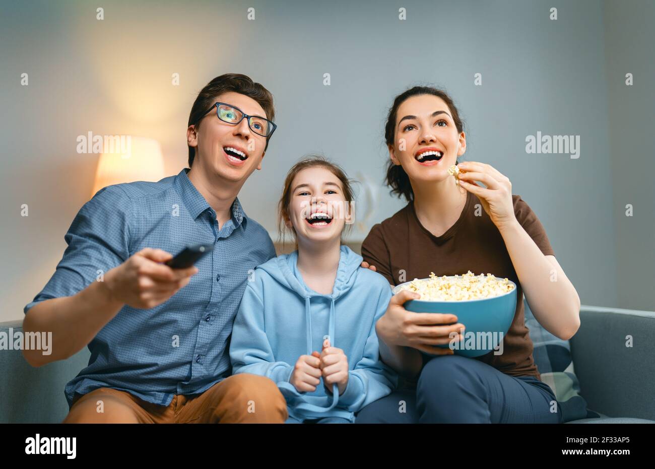 Happy family watching projector, TV, movies with popcorn in the evening ...