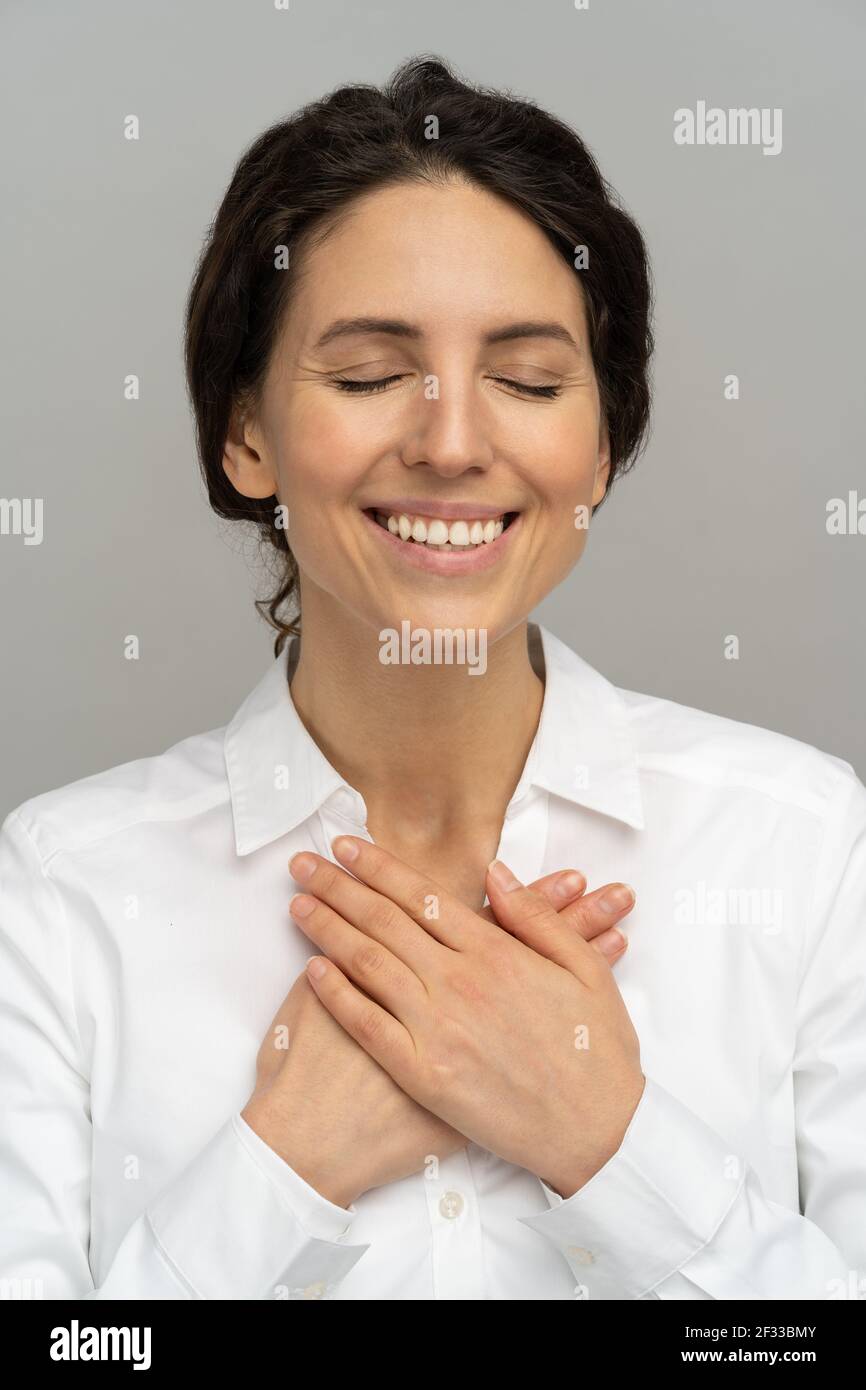 Friendly woman holds hands on chest, feels grateful for love ...