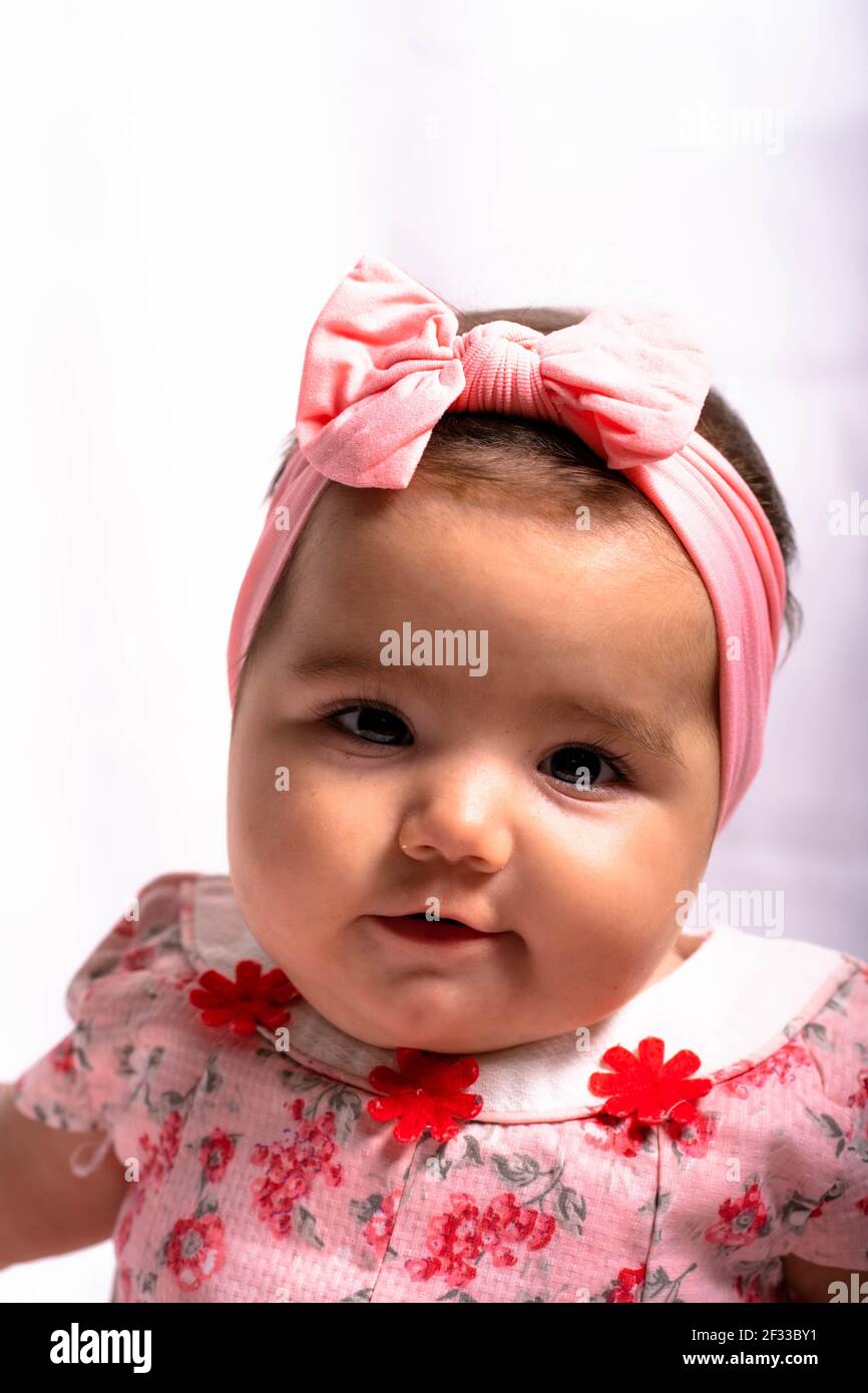 An adorable Hispanic baby wearing a pink floral dress against a white ...