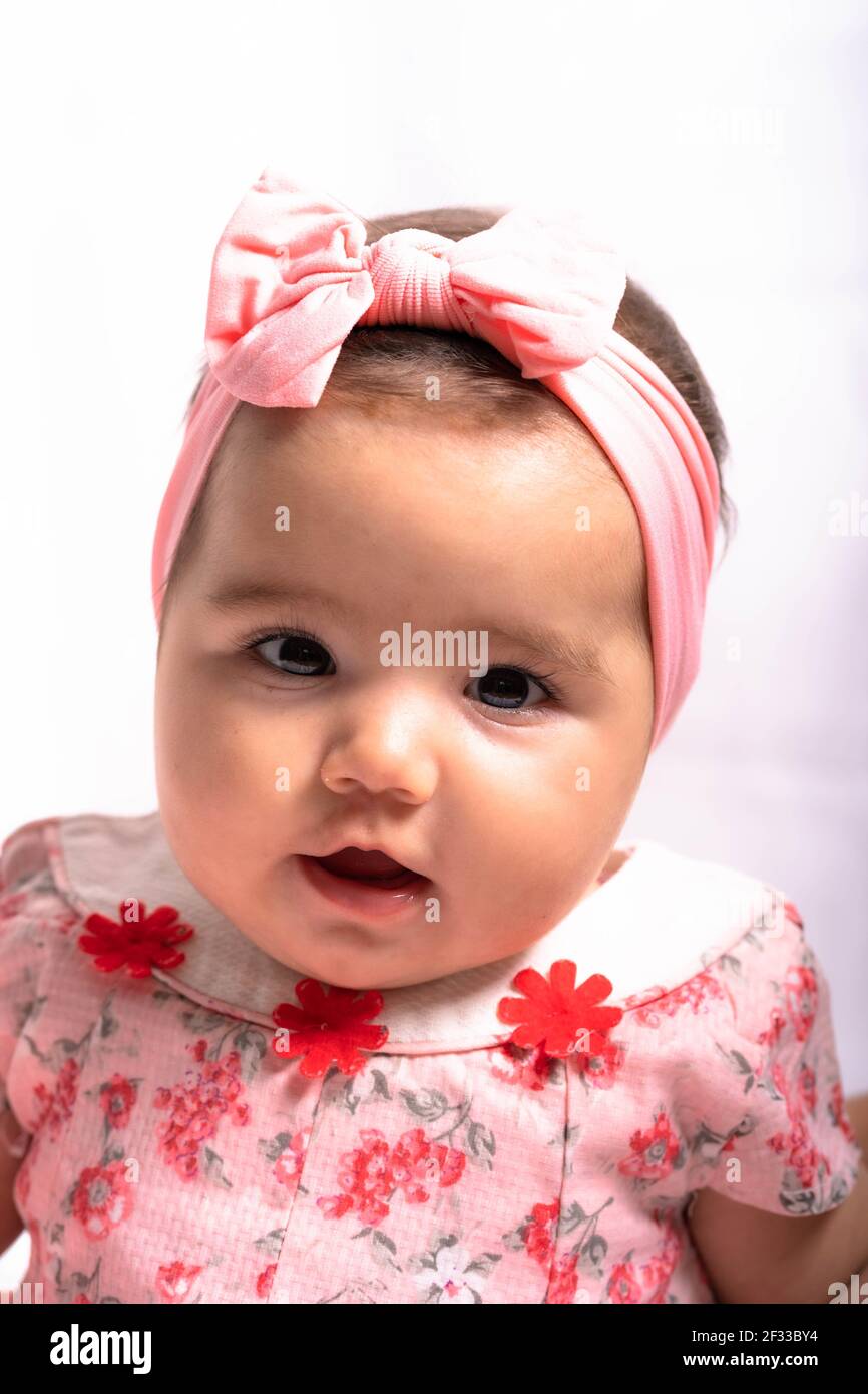 An adorable Hispanic baby wearing a pink floral dress against a white ...